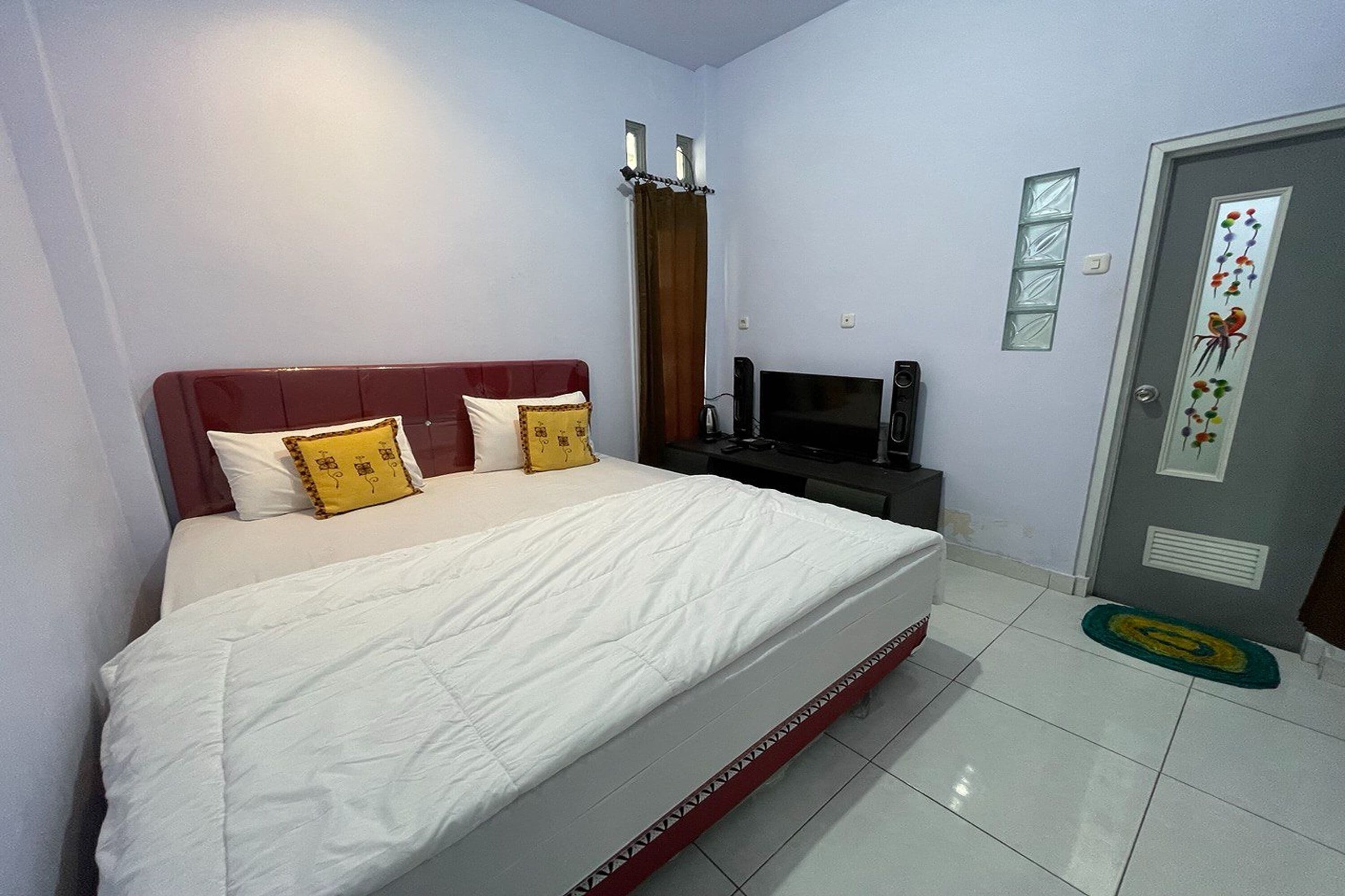 Quarto com uma cama grande, televisão e porta com painéis de vidro decorativos.