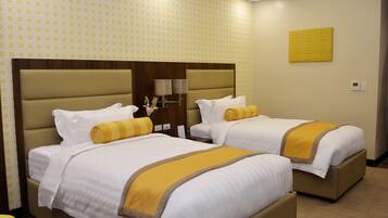 Quarto de hotel com duas camas, cada uma com cabeceira, roupa de cama branca e detalhes amarelos.