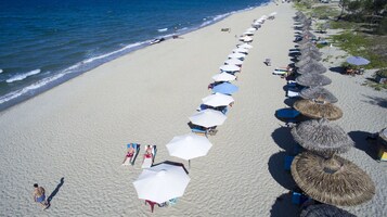 Uma praia com fileiras de guarda-sóis e cadeiras de praia, uma faixa de areia e o oceano.