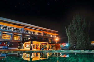 Um hotel com vários andares, piscina, área de estar externa e uma grande árvore.