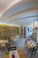 Uma sala de jantar espaçosa com parede de pedra, mesas e cadeiras de madeira. Uma escada leva a outro andar.