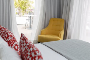 Quarto de hotel com uma cama, uma poltrona amarela e vista para o exterior.