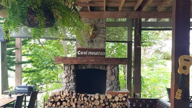 Um pátio externo com lareira de pedra, vigas de madeira e um letreiro com a inscrição 'Cool Mountain'.