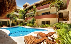 Uma área de piscina com espreguiçadeiras e um edifício com telhado de palha.