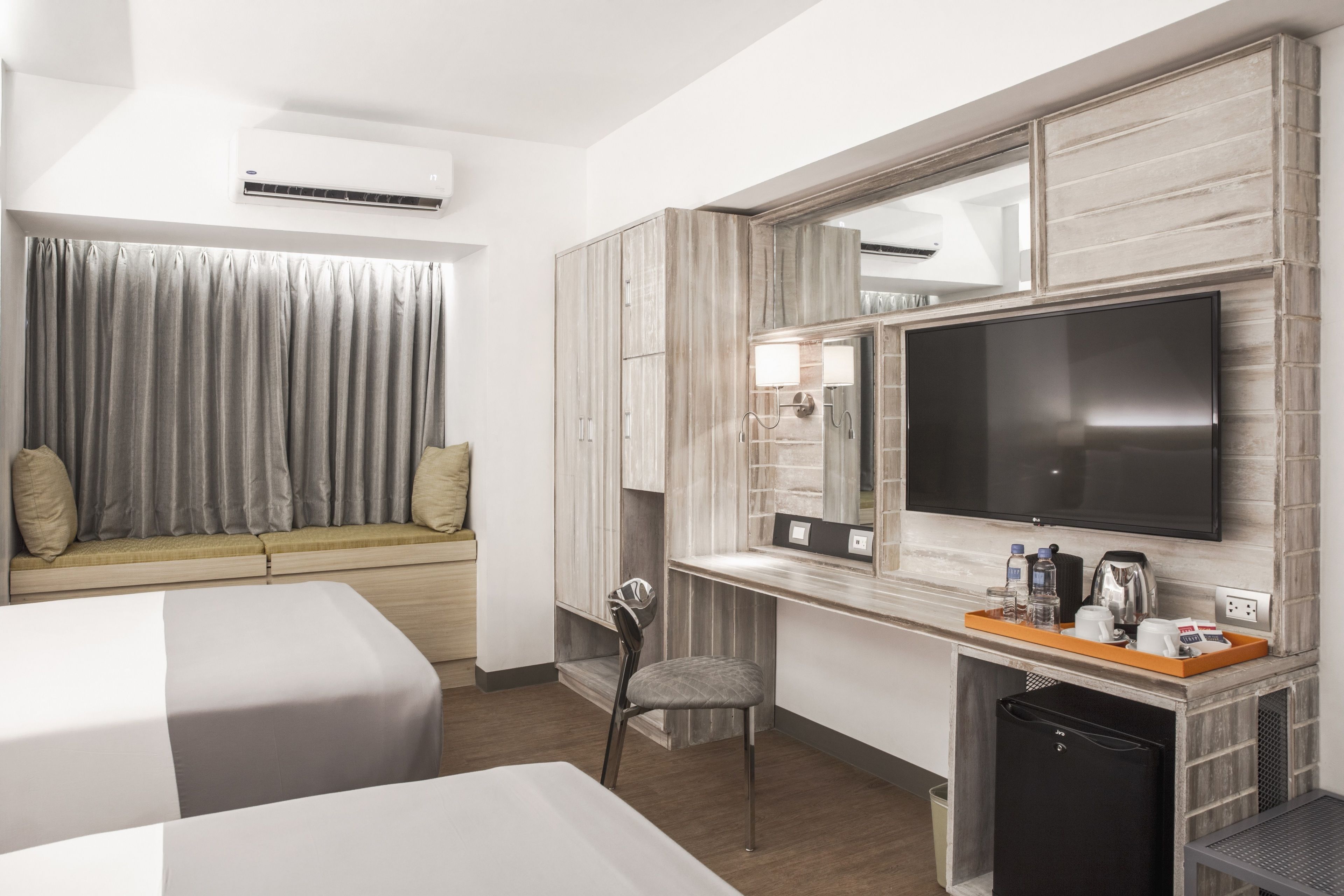 Quarto de hotel com duas camas, uma secretária, televisão de ecrã plano, uma kitchenette pequena e uma janela com cortinas.