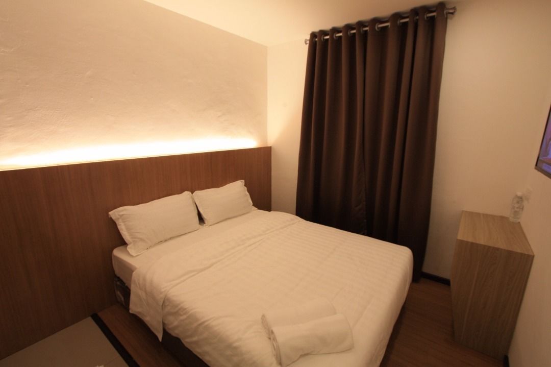 Cama bem arrumada com lençóis brancos, cabeceira de madeira e luminária fixada na parede.
