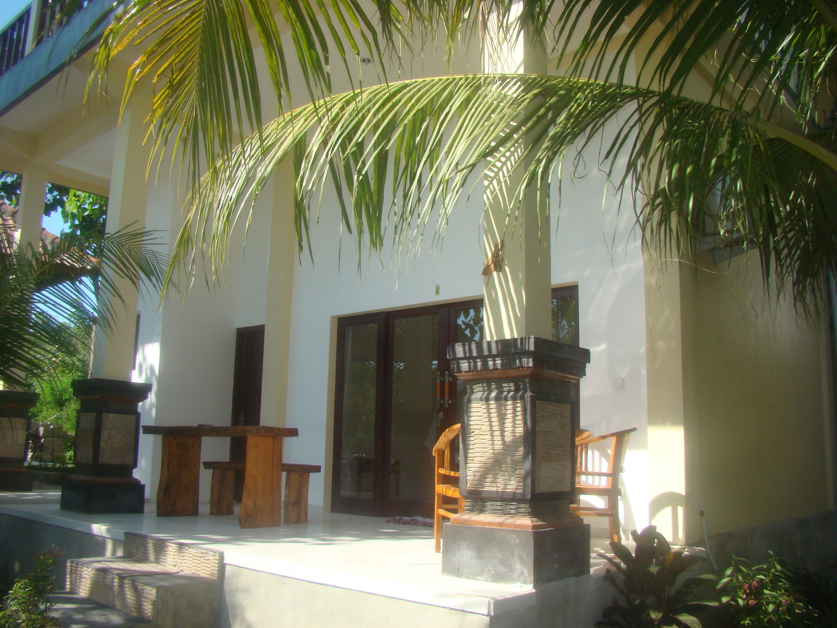 Uma área externa coberta com um banco de madeira, uma mesa e uma palmeira.