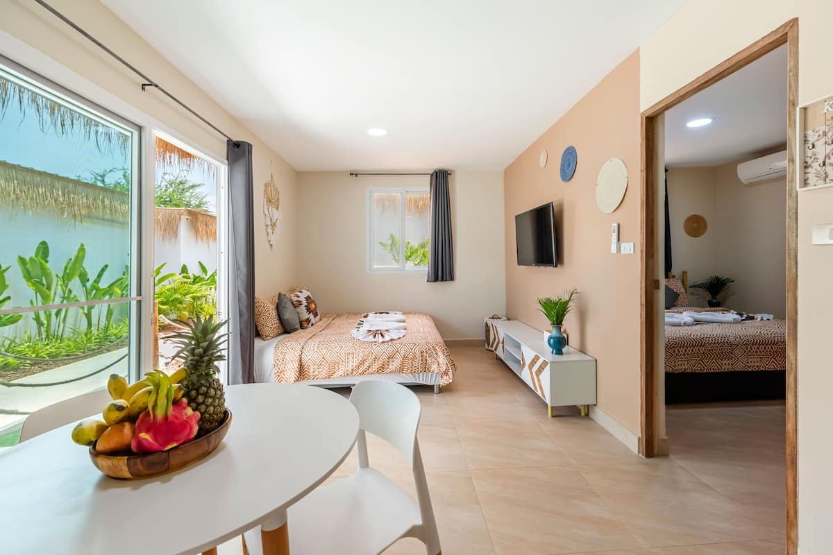 Quarto de hotel moderno com cama, escrivaninha, televisão e uma janela grande com vista para o verde.