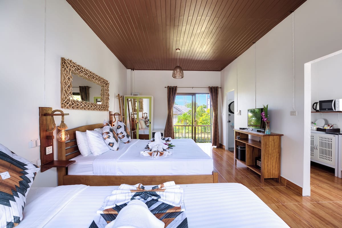 Quarto de hotel com duas camas, cabeceiras de madeira, um espelho grande, teto de madeira, área de refeições com micro-ondas e vista para o verde lá fora.