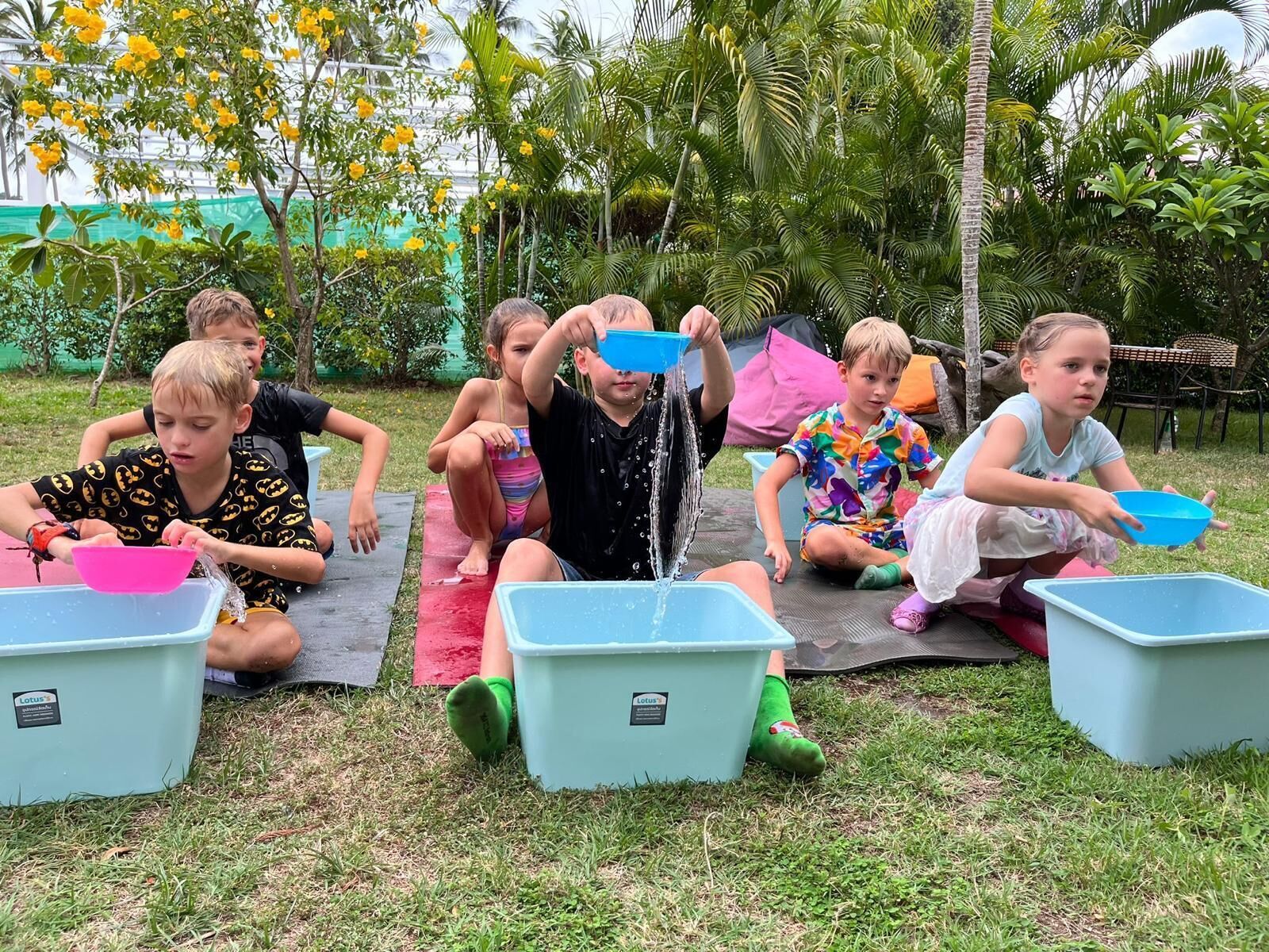 Crianças brincando com recipientes de água ao ar livre.