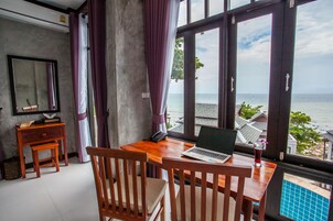 Quarto com escrivaninha de madeira, laptop e vista para o mar.