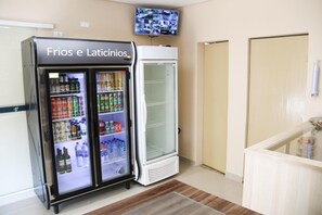 Mini-bar com geladeira identificada como 'Fríos e Latínicos', contendo diversas bebidas.