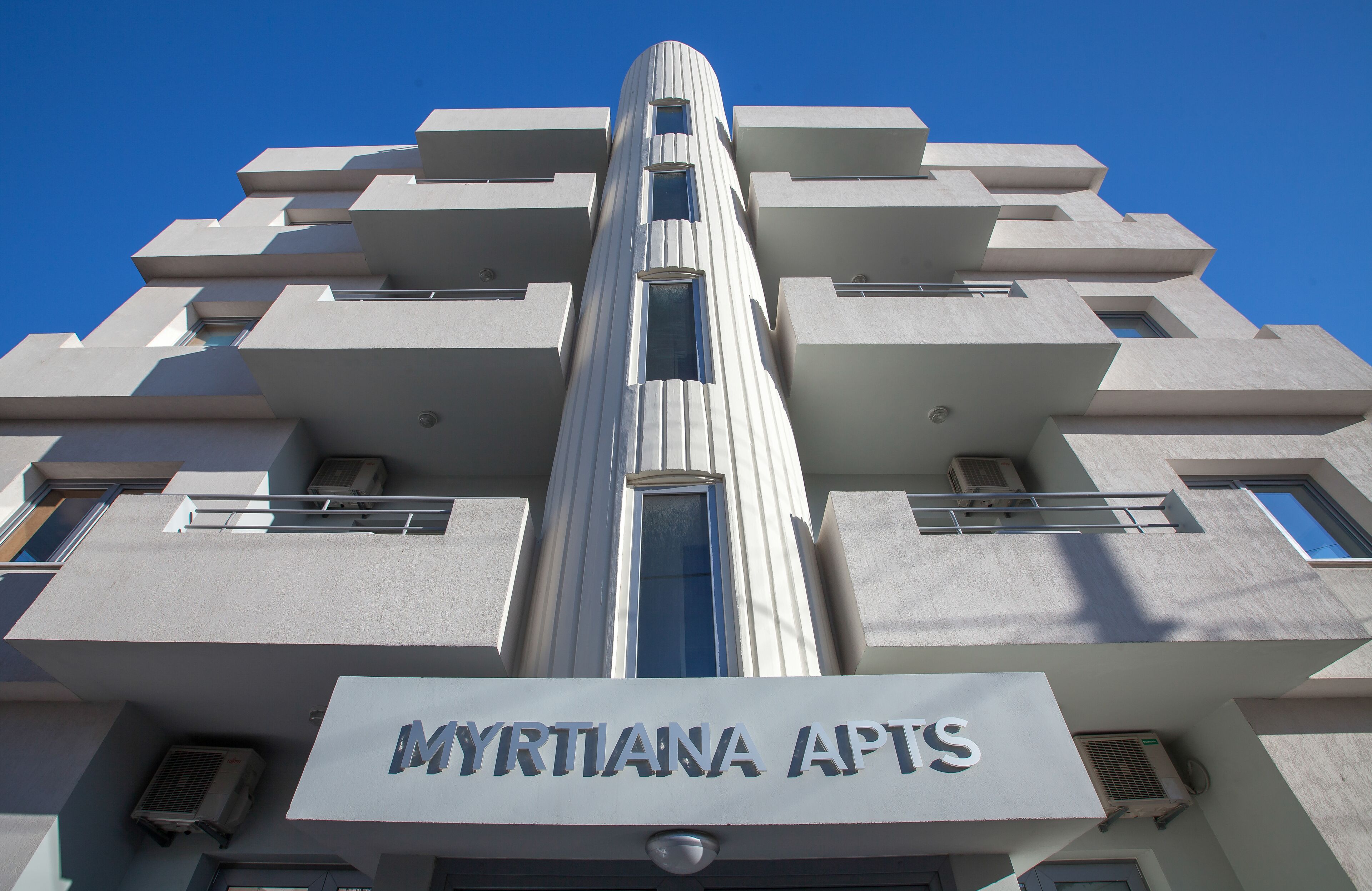 Um edifício moderno com um elemento vertical central e várias varandas.