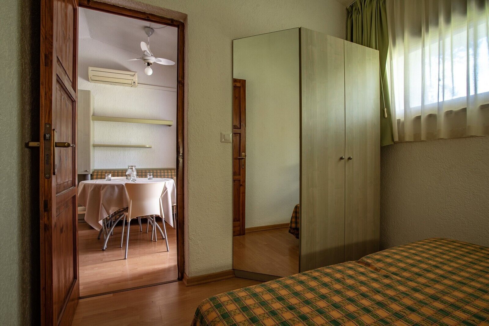 Um quarto com uma cama, uma mesa com cadeiras, um guarda-roupa e um ventilador de teto.