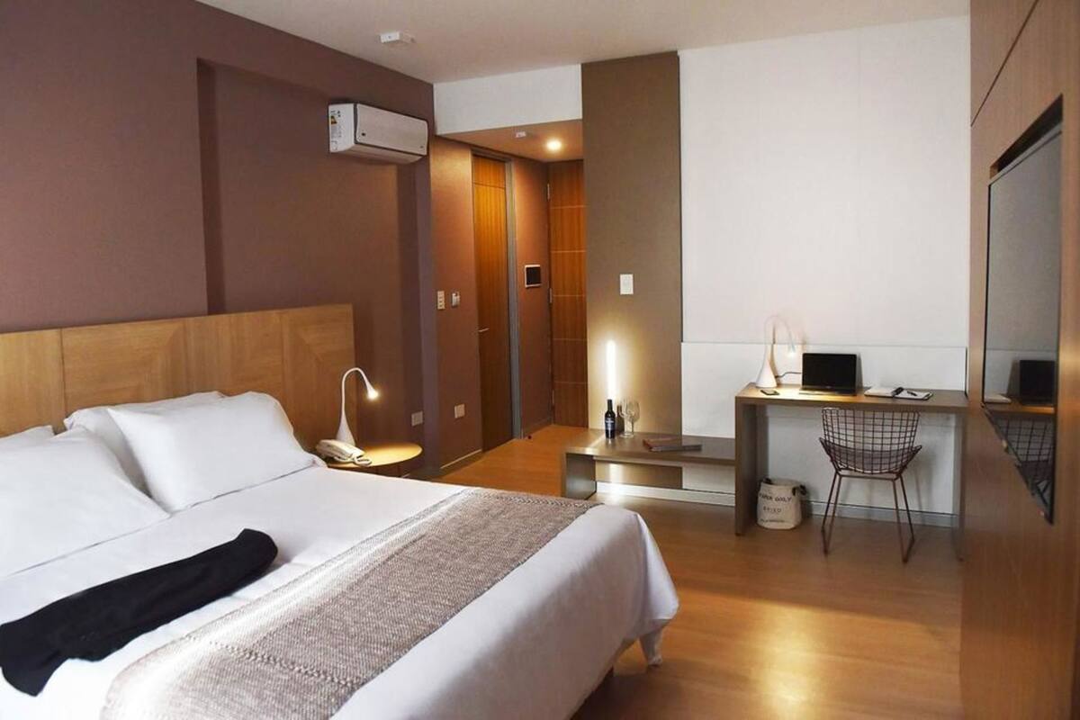 Quarto de hotel com cama, escrivaninha, cadeira e espelho.
