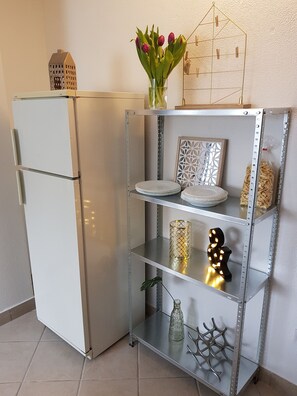 Uma cozinha com geladeira branca, um armário de metal com objetos decorativos e um pequeno modelo de casa no topo.