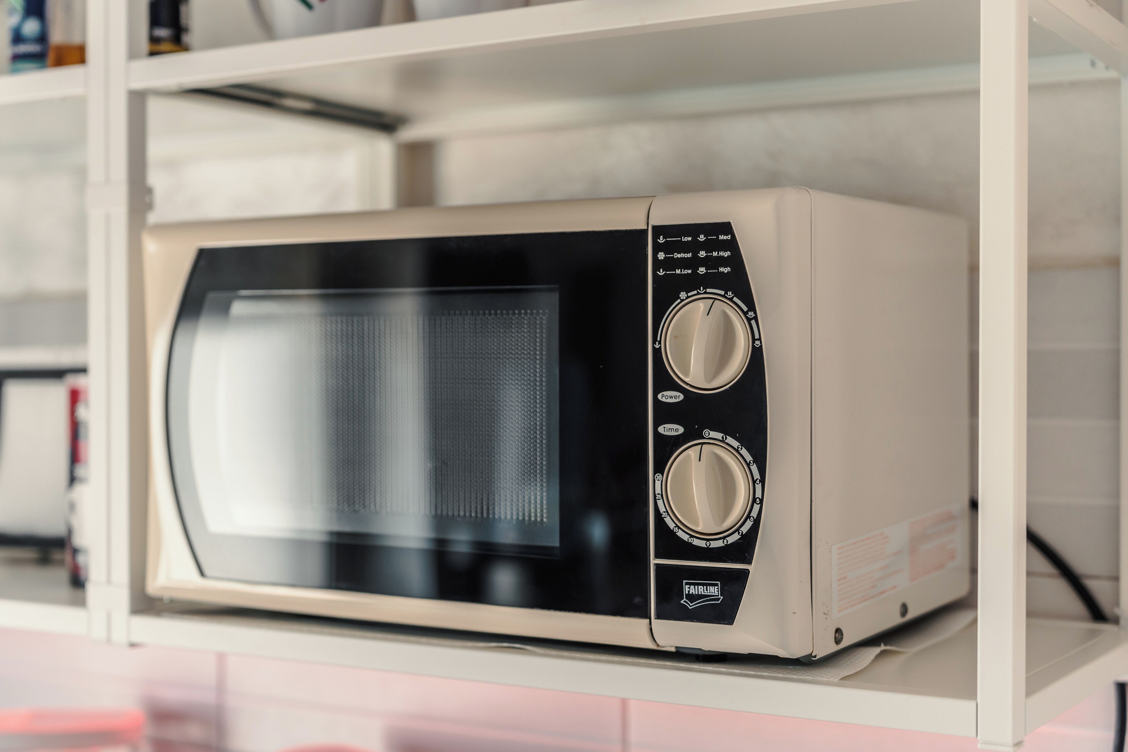 Forno de micro-ondas fixado numa prateleira branca com painel de controle que inclui configurações de temperatura e botão de energia.
