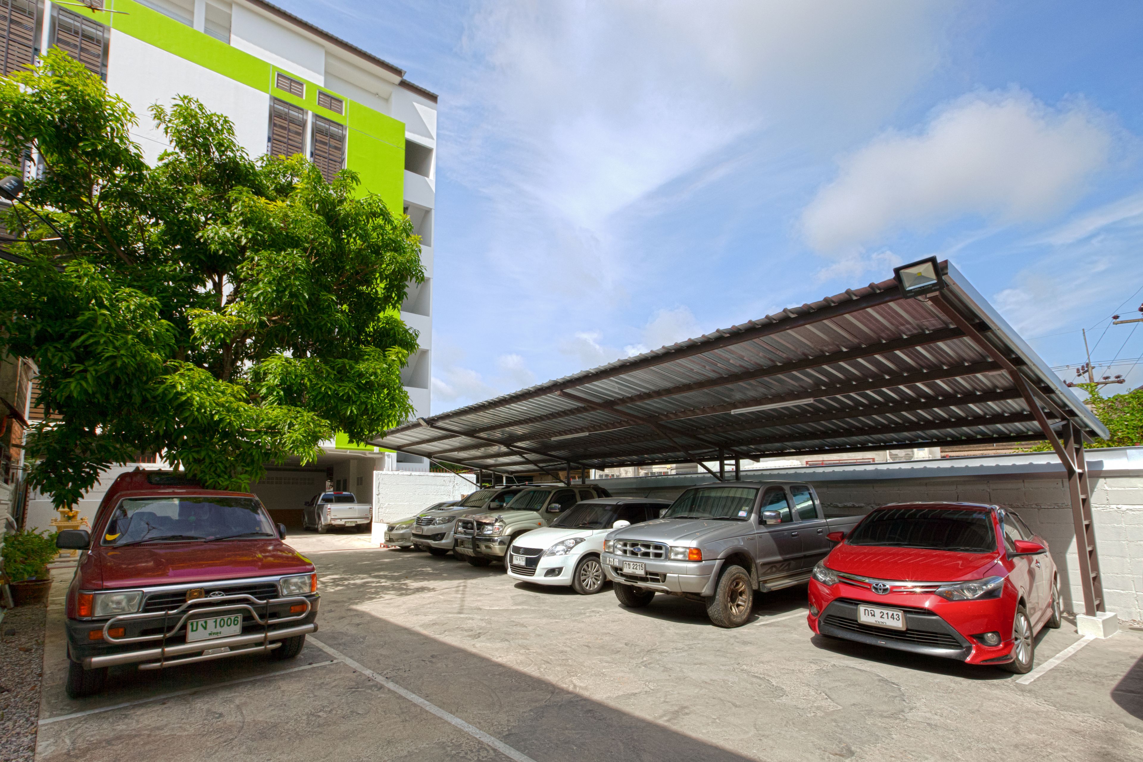 Uma área de estacionamento com vários carros, uma cobertura e um edifício com fachada verde e branca.