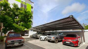 Uma área de estacionamento com vários carros, uma cobertura e um edifício com fachada verde e branca.
