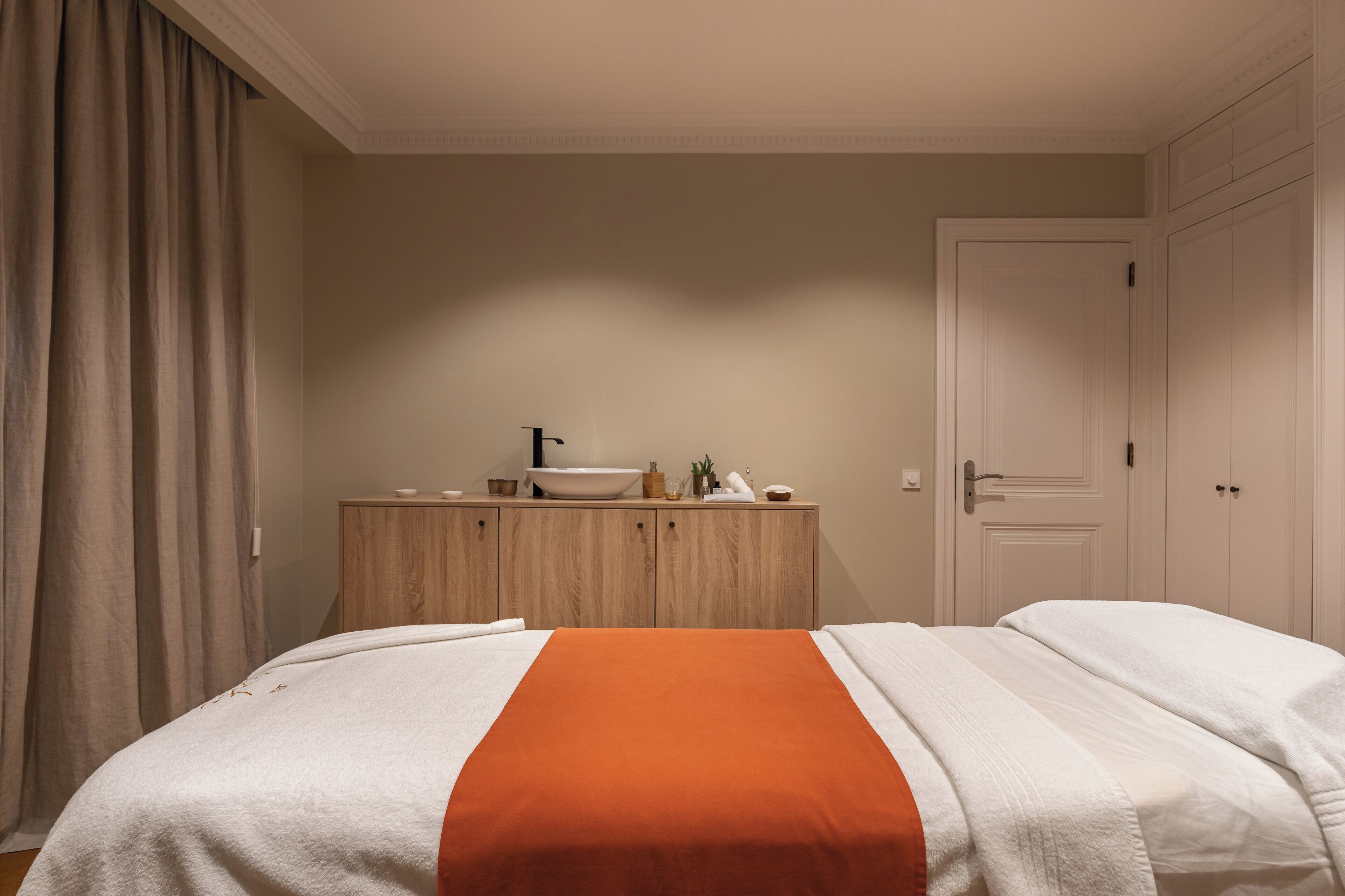 Quarto de hotel com uma cama, cómoda de madeira, pia e porta.