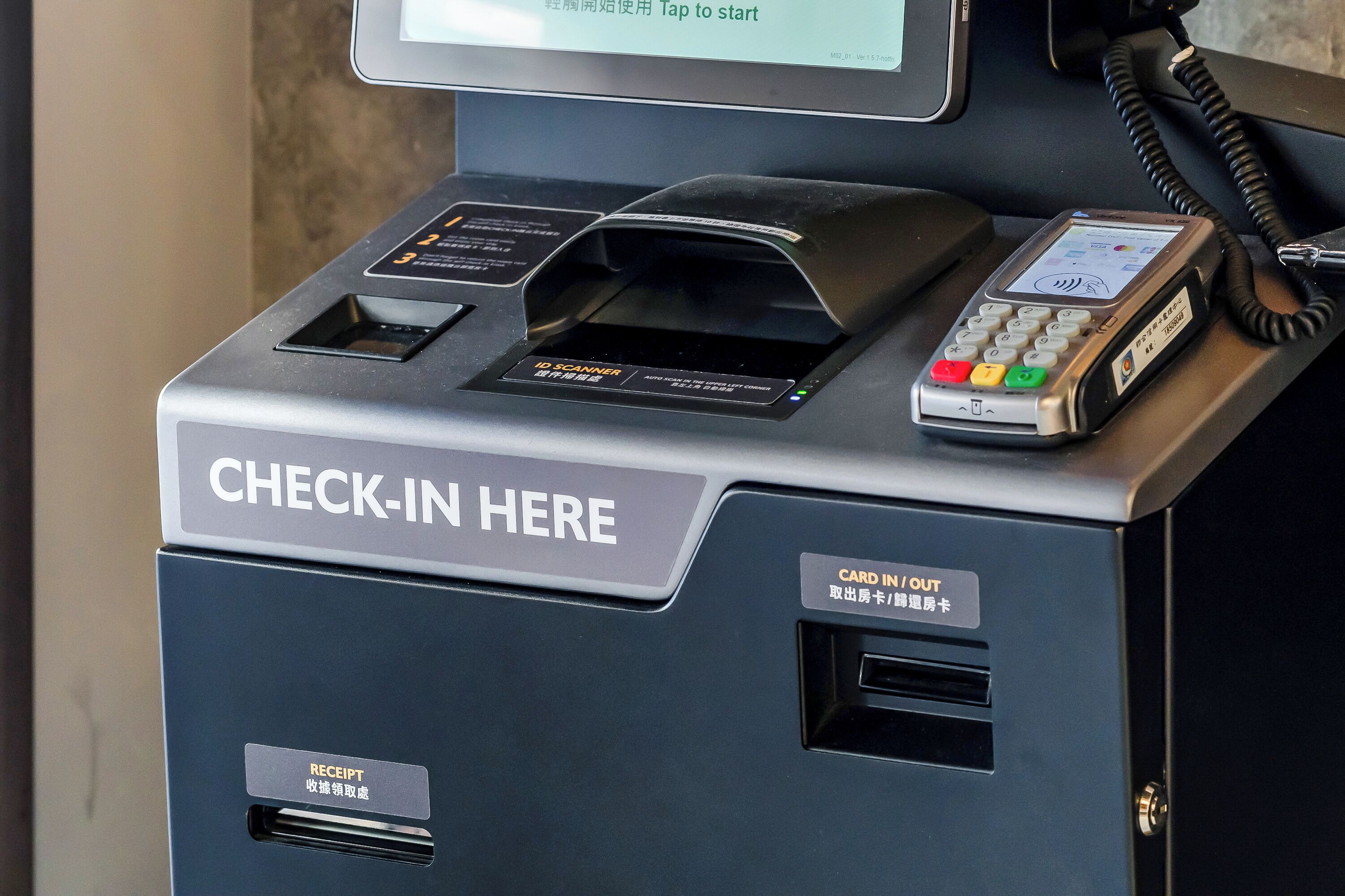 Um quiosque de check-in com leitor de cartão, um telefone e uma tela exibindo instruções.