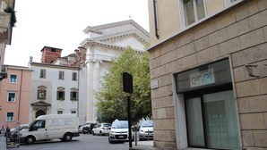 Cena de rua com uma van branca estacionada na lateral, um edifício com a placa 'enet' à direita e uma árvore ao fundo.