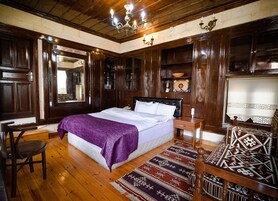Quarto tradicional com uma cama grande, paredes de madeira, um candelabro e um tapete estampado.