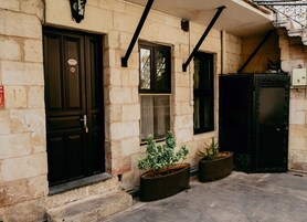 Fachada de edifício com porta preta, janela e portão preto. Há duas plantas em vasos à frente.