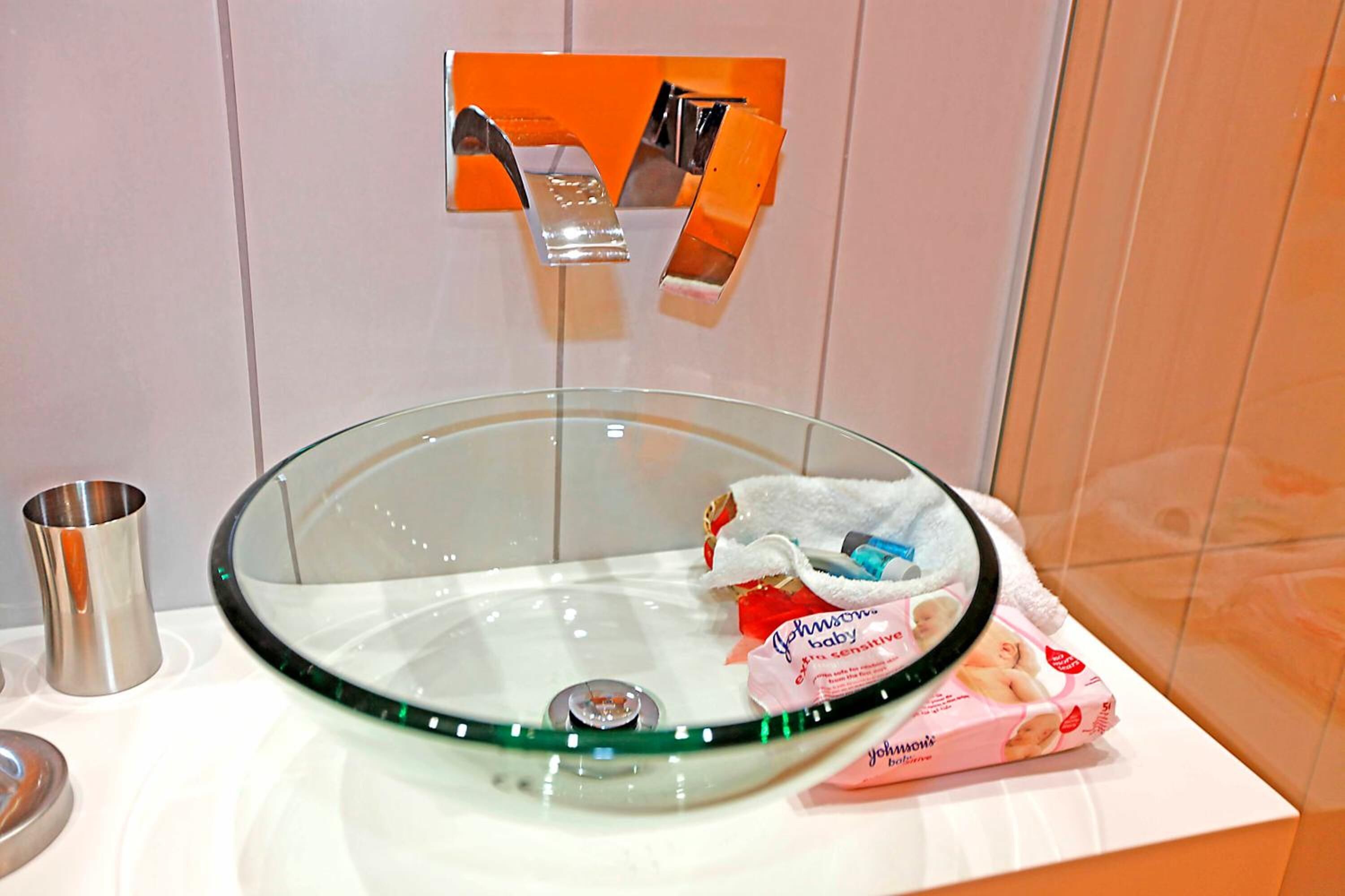 Uma casa de banho com lavatório de vidro, torneira metálica e uma caixa de lenços no balcão.