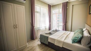 Quarto de hotel com cama, guarda-roupa e janela com cortinas.