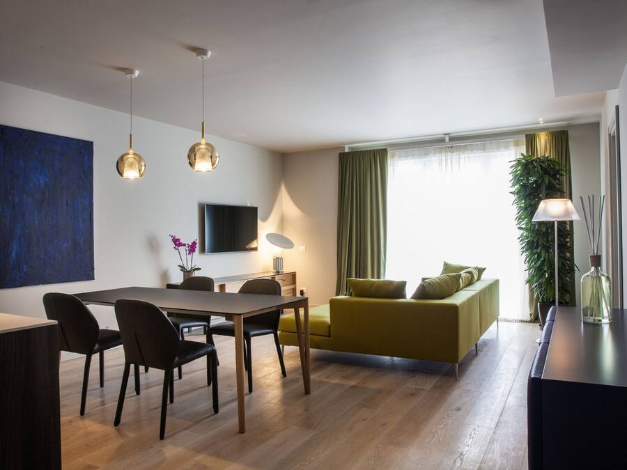 Uma sala de estar moderna com área de jantar, sofá e televisão fixada na parede.