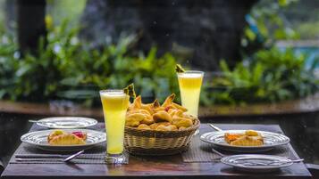 Uma mesa com pratos de comida, um cesto de doces e dois copos de uma bebida amarela.