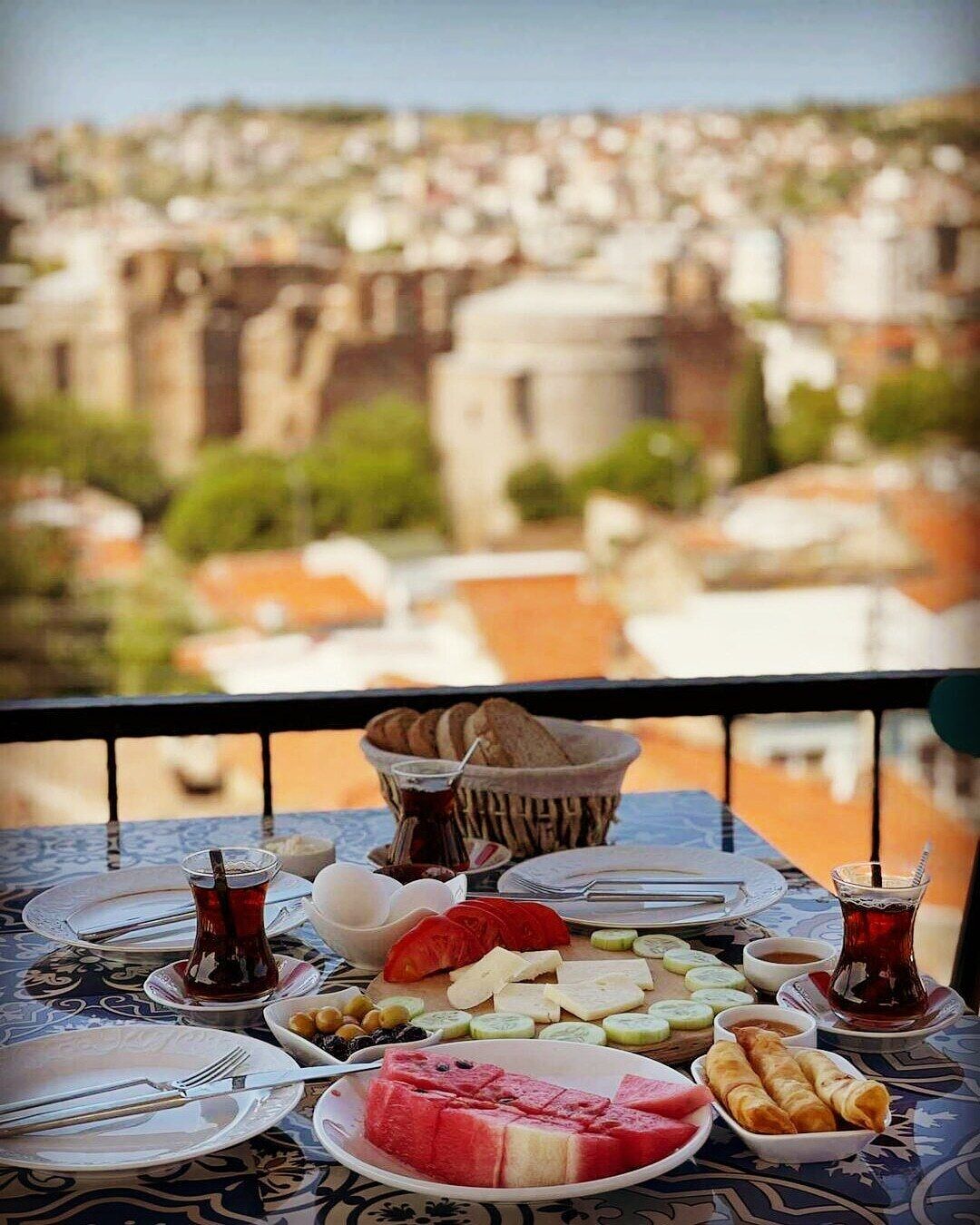 Mesa posta para o pequeno-almoço com várias comidas e bebidas, com vista para a paisagem urbana.