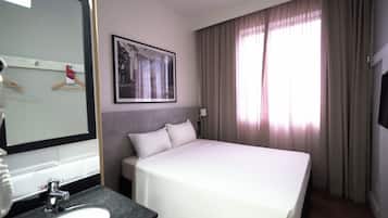 Quarto de hotel com uma cama, um espelho grande, uma pia e uma janela com cortinas.