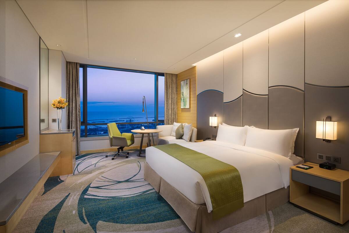 Quarto de hotel com uma cama grande, uma escrivaninha, uma cadeira, uma mesinha e vista para o mar.