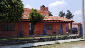 Um edifício residencial com telhado de telhas vermelhas, chaminé de tijolos e cerca de arame.