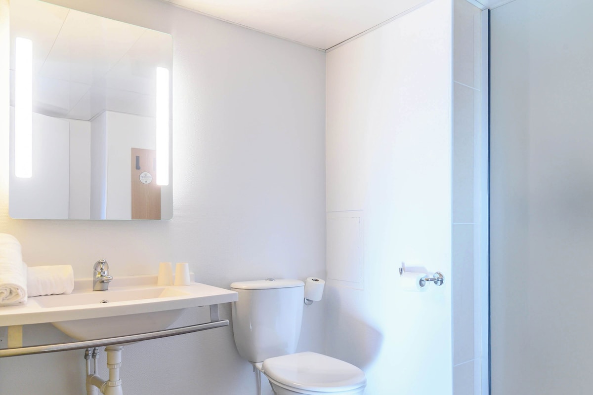 Casa de banho moderna com lavatório, sanita e chuveiro, tudo em branco.