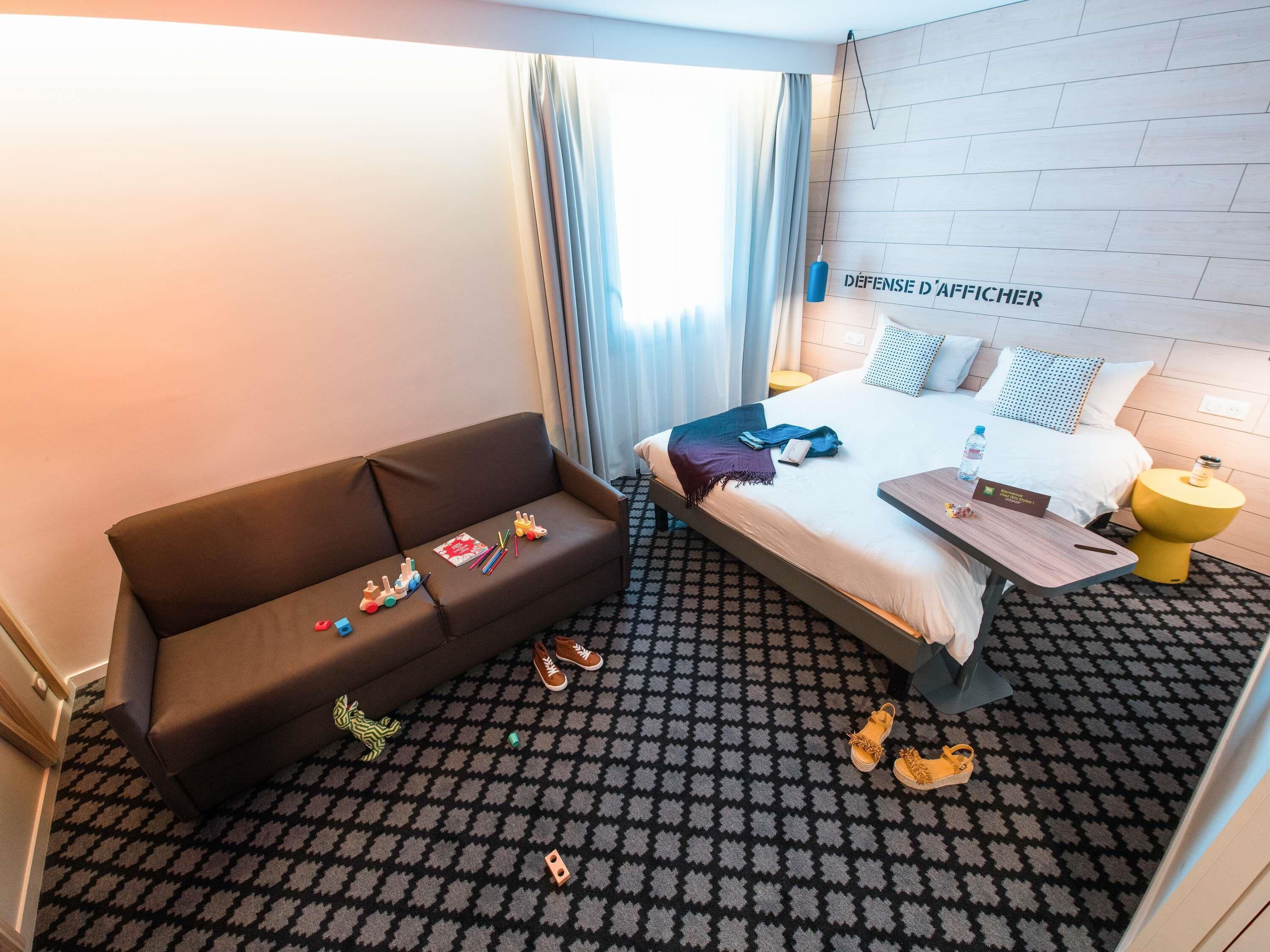 Quarto de hotel com uma cama, um sofá, uma mesa pequena e um tapete estampado.
