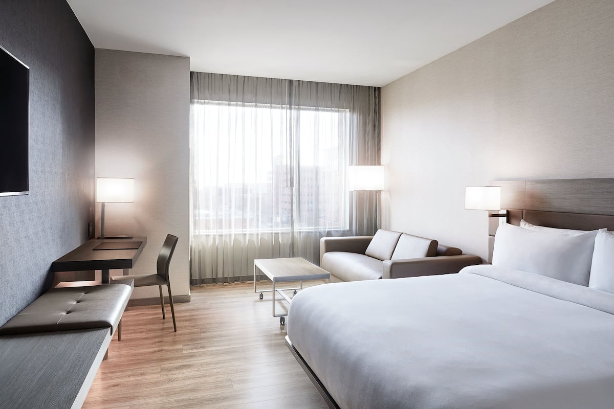 Quarto de hotel moderno com uma cama grande, uma escrivaninha, uma cadeira, um sofá e uma mesinha.