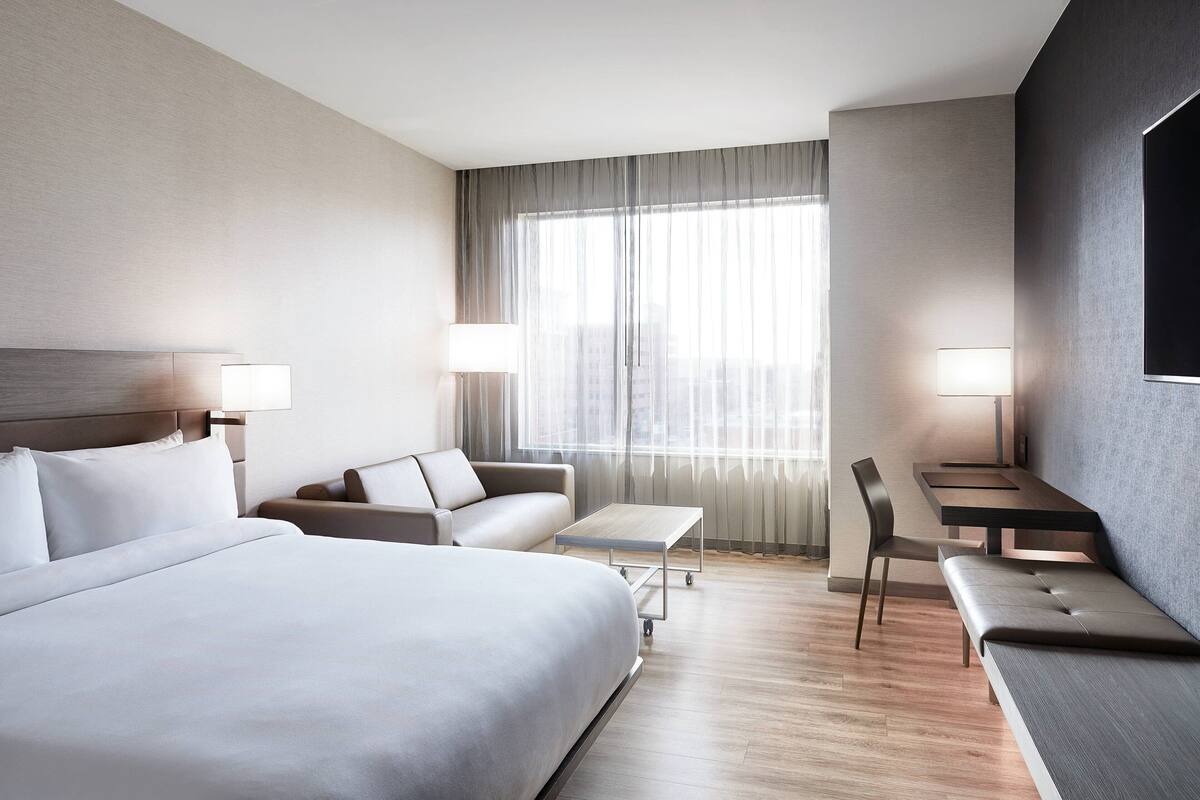 Quarto de hotel moderno com uma cama grande, um sofá, uma mesinha e uma escrivaninha.