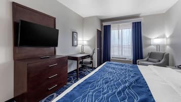 Quarto de hotel com uma cama, uma escrivaninha com cadeira, uma televisão e duas luminárias.