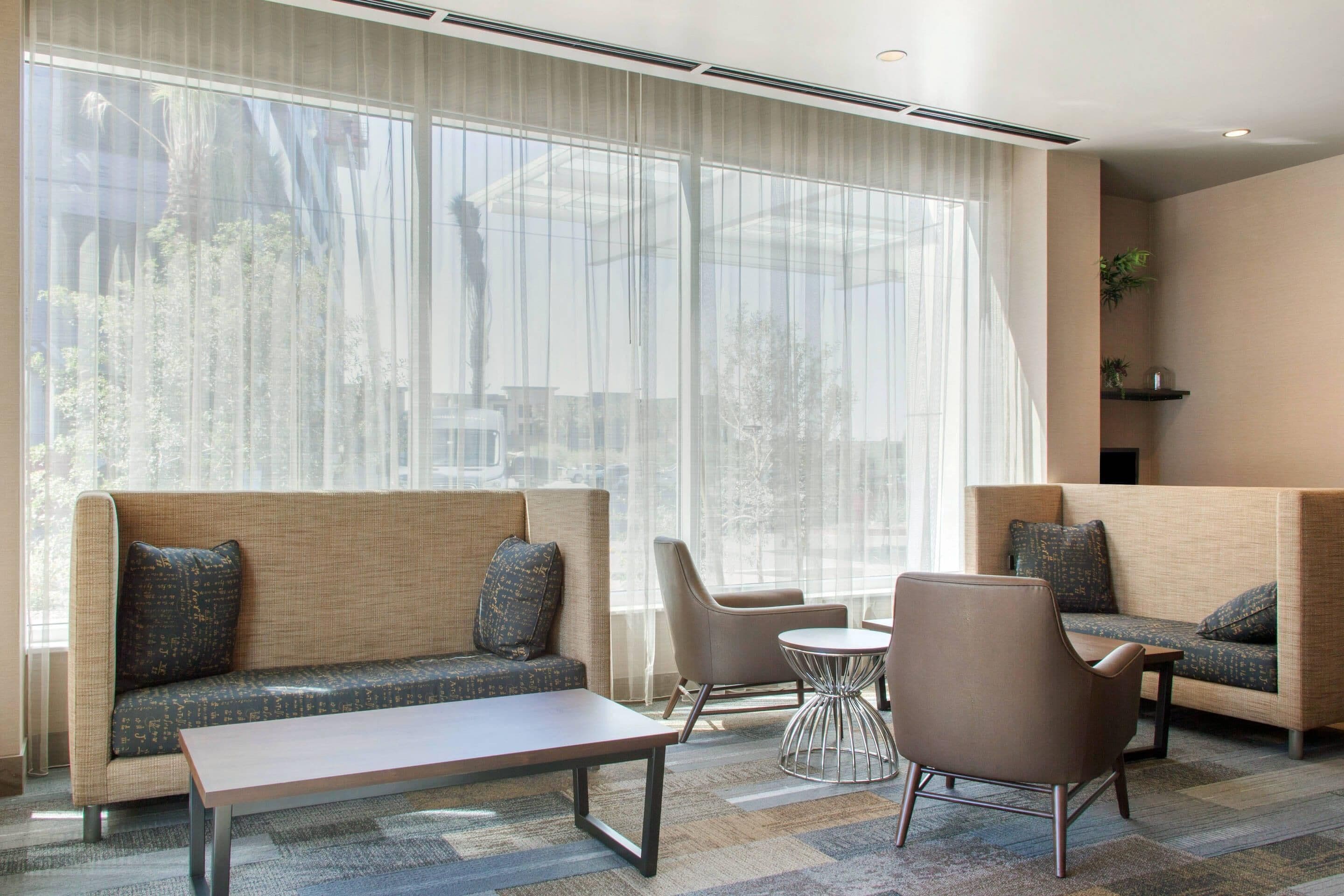 Um lobby de hotel moderno com um sofá, poltronas, uma mesa de centro e janelas amplas.