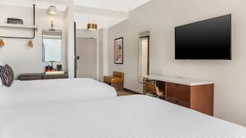 Quarto de hotel moderno com uma cama grande, uma escrivaninha, uma cadeira, uma TV de tela plana e um espelho.