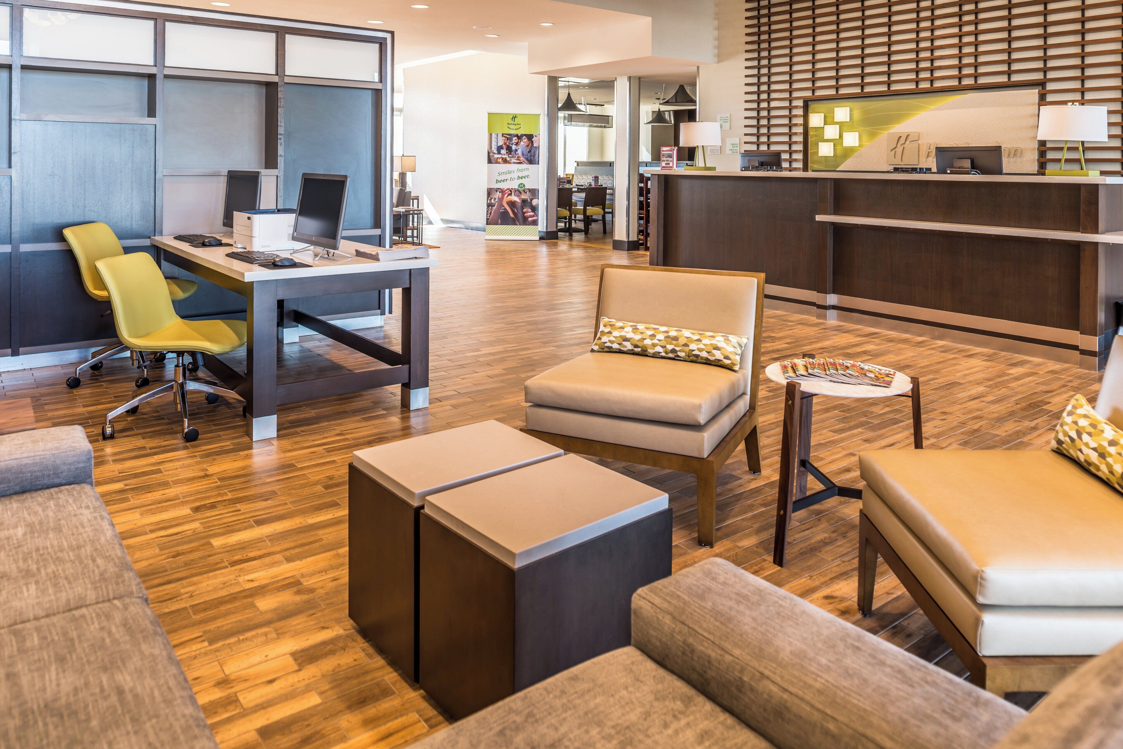Um hall de hotel moderno com balcão de recepção, área de estar e posto de computadores.