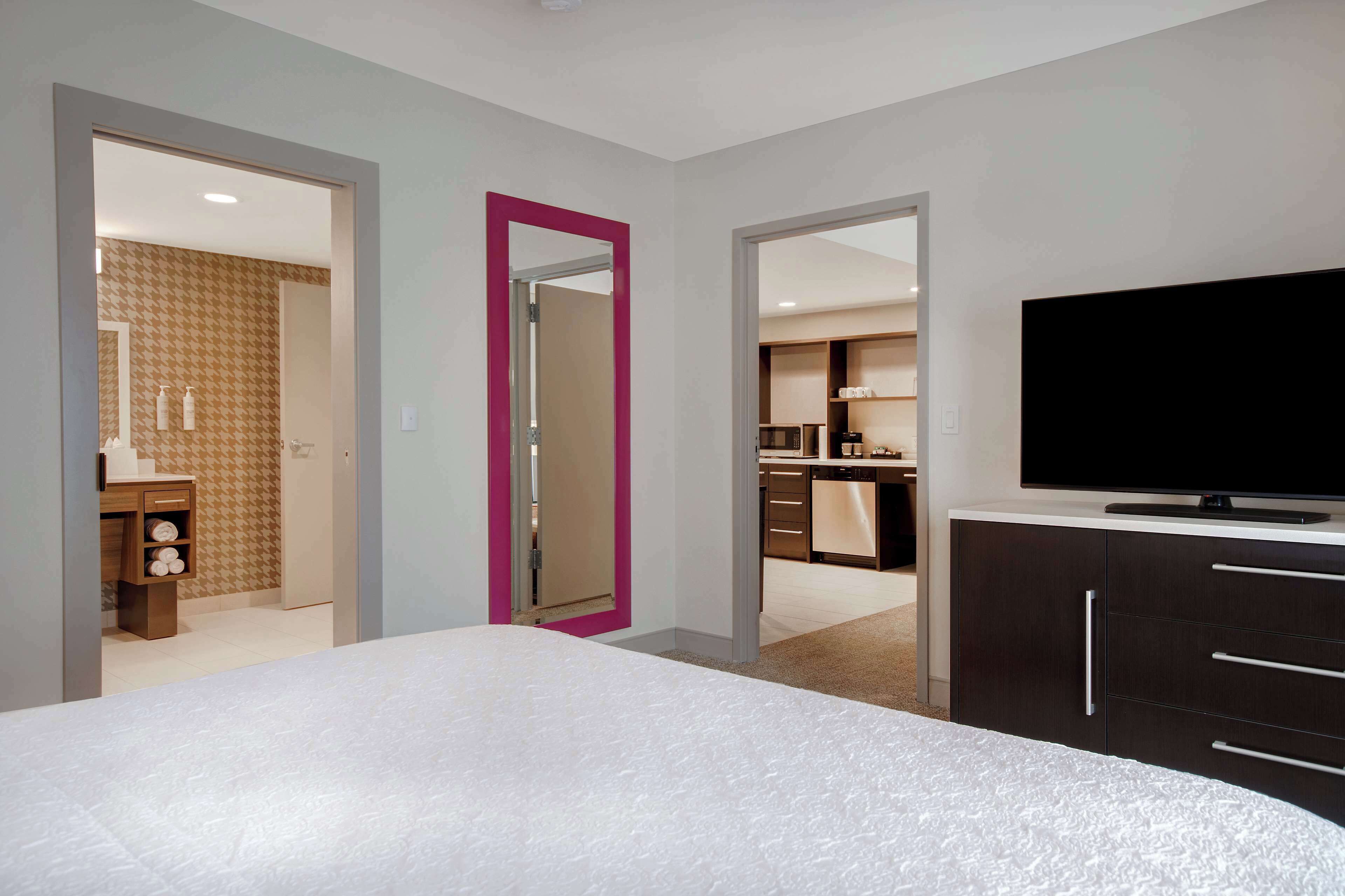 Quarto de hotel moderno com uma cama grande, uma televisão de tela plana, um guarda-roupa e vista para a área da cozinha.
