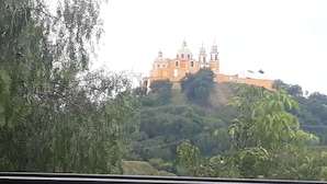 Vista de um edifício no topo da colina com várias cúpulas e torres, rodeado por vegetação e árvores.