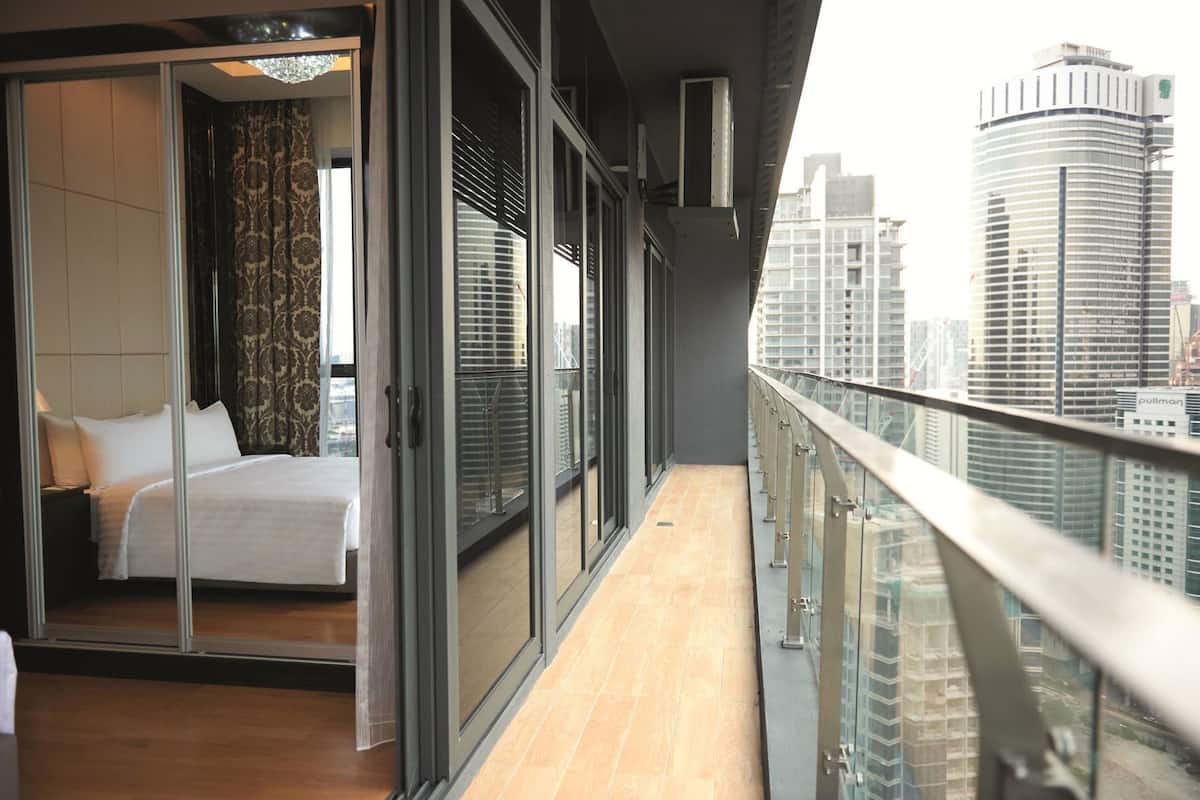 Quarto de hotel moderno com cama, portas de correr de vidro e varanda com vista para a paisagem urbana.