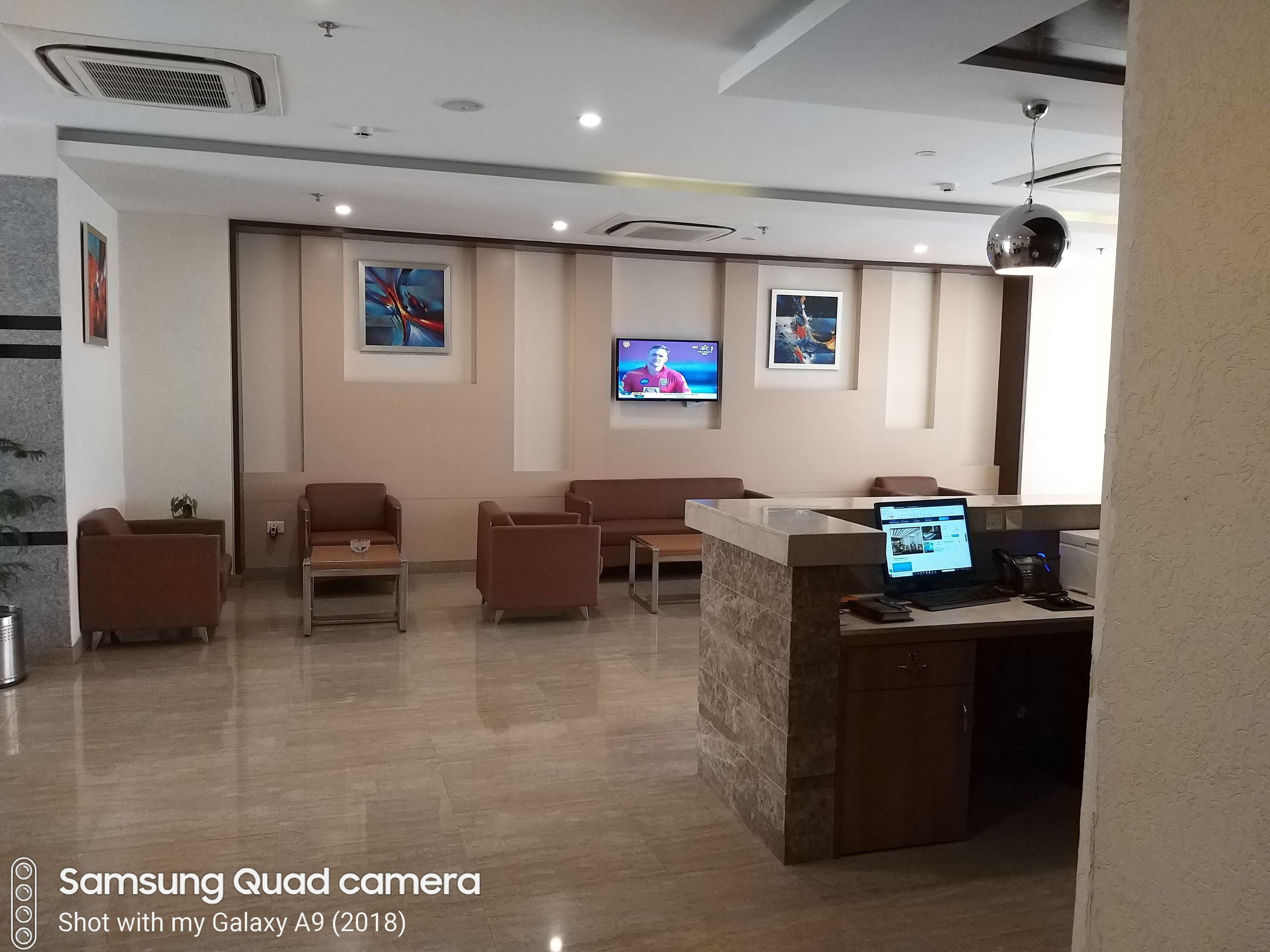 Uma área de recepção com balcão, cadeiras e uma tela de televisão.