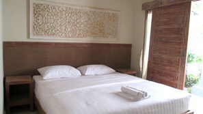 Quarto de hotel com uma cama grande, duas almofadas, cabeceira de madeira, mesa de cabeceira e porta de madeira.