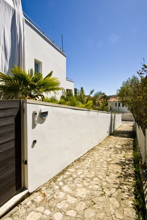 Um caminho de pedra estreito que leva a um edifício moderno branco, com uma porta escura e uma pequena janela.